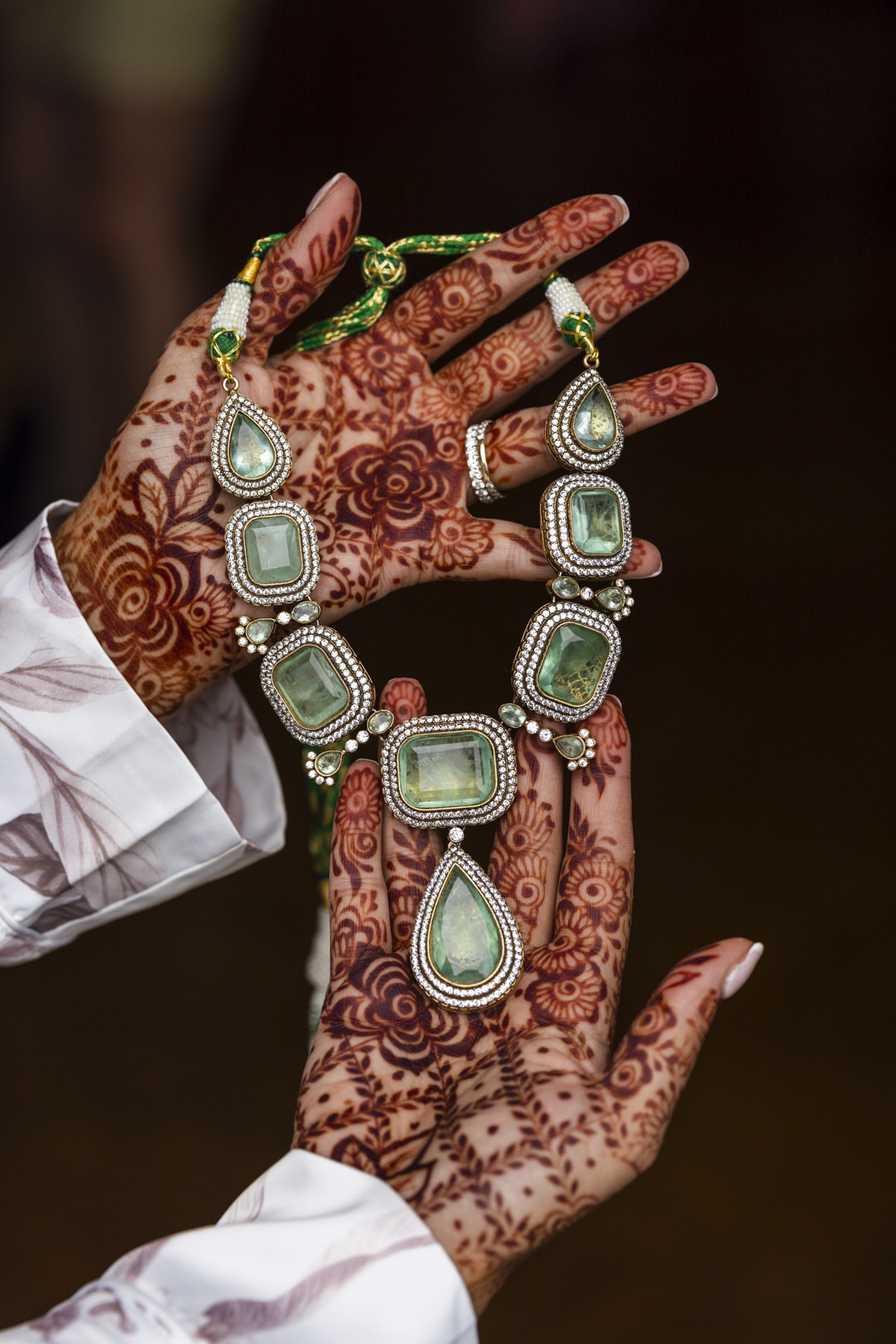 Hands adorned with intricate henna designs hold a striking necklace ...