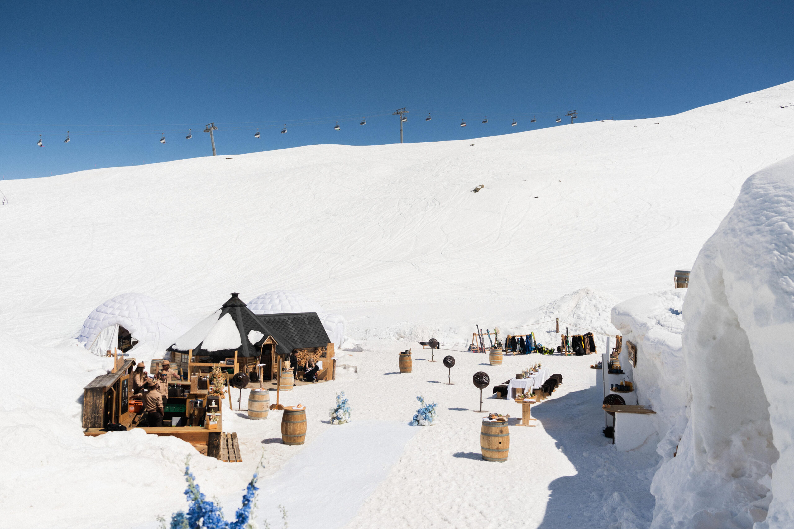 A snow-covered outdoor seating area with wooden tables and barrel ...