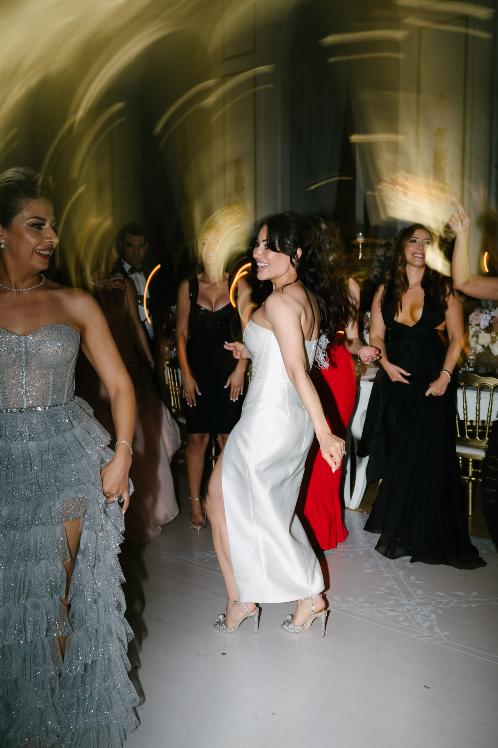 A group of women in formal dresses dance joyfully at an indoor event at ...