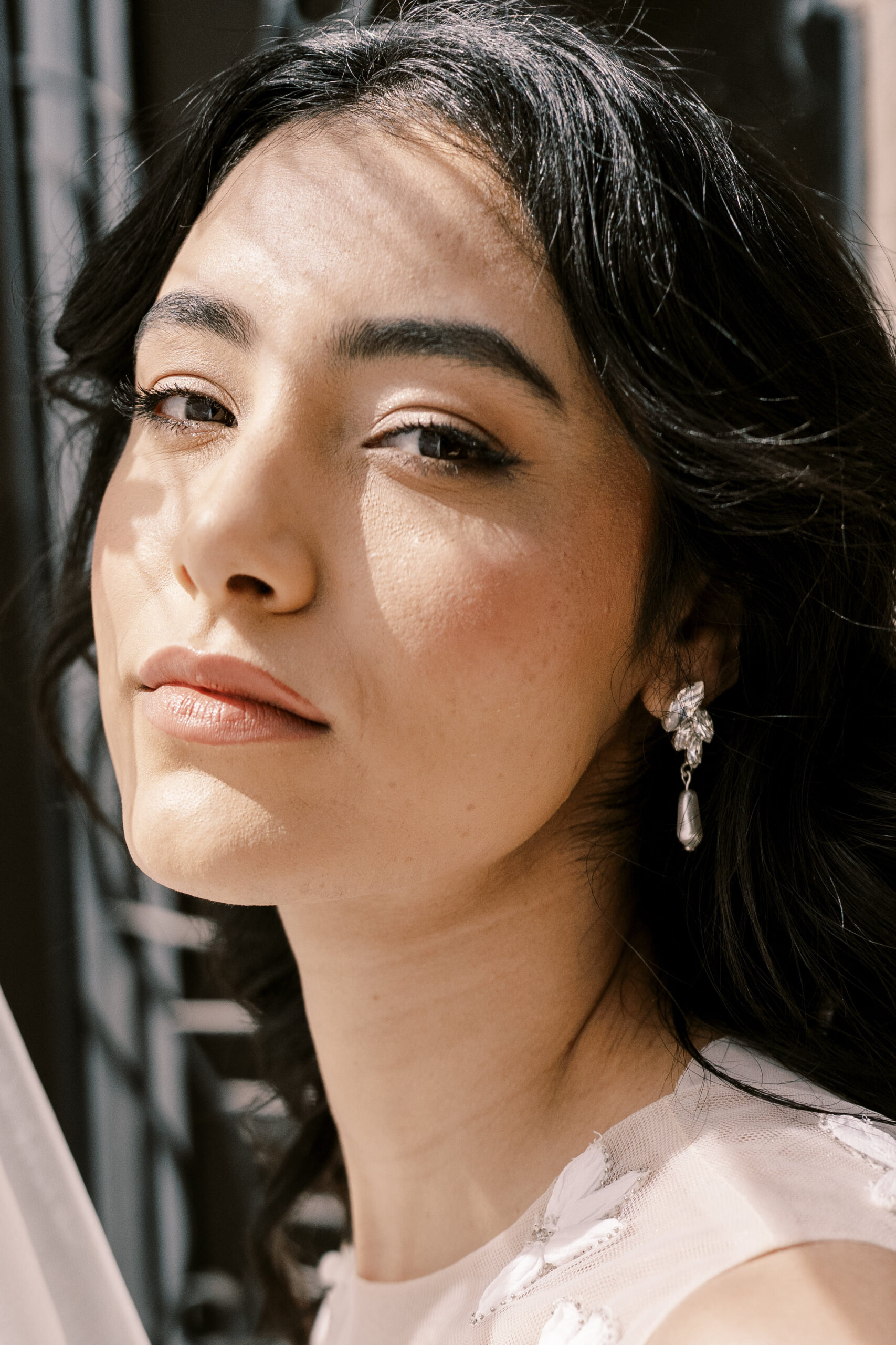 A woman with wavy dark hair and light makeup looks confidently at the ...