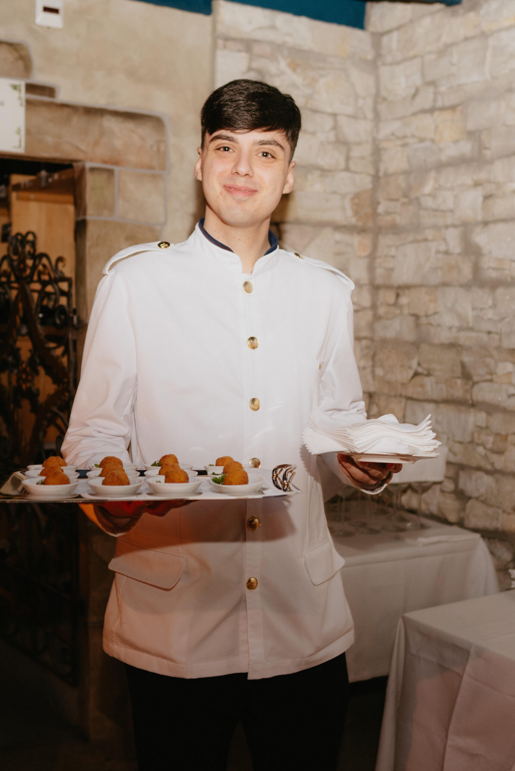 A young waiter in a white uniform holds a tray of appetizers and a ...