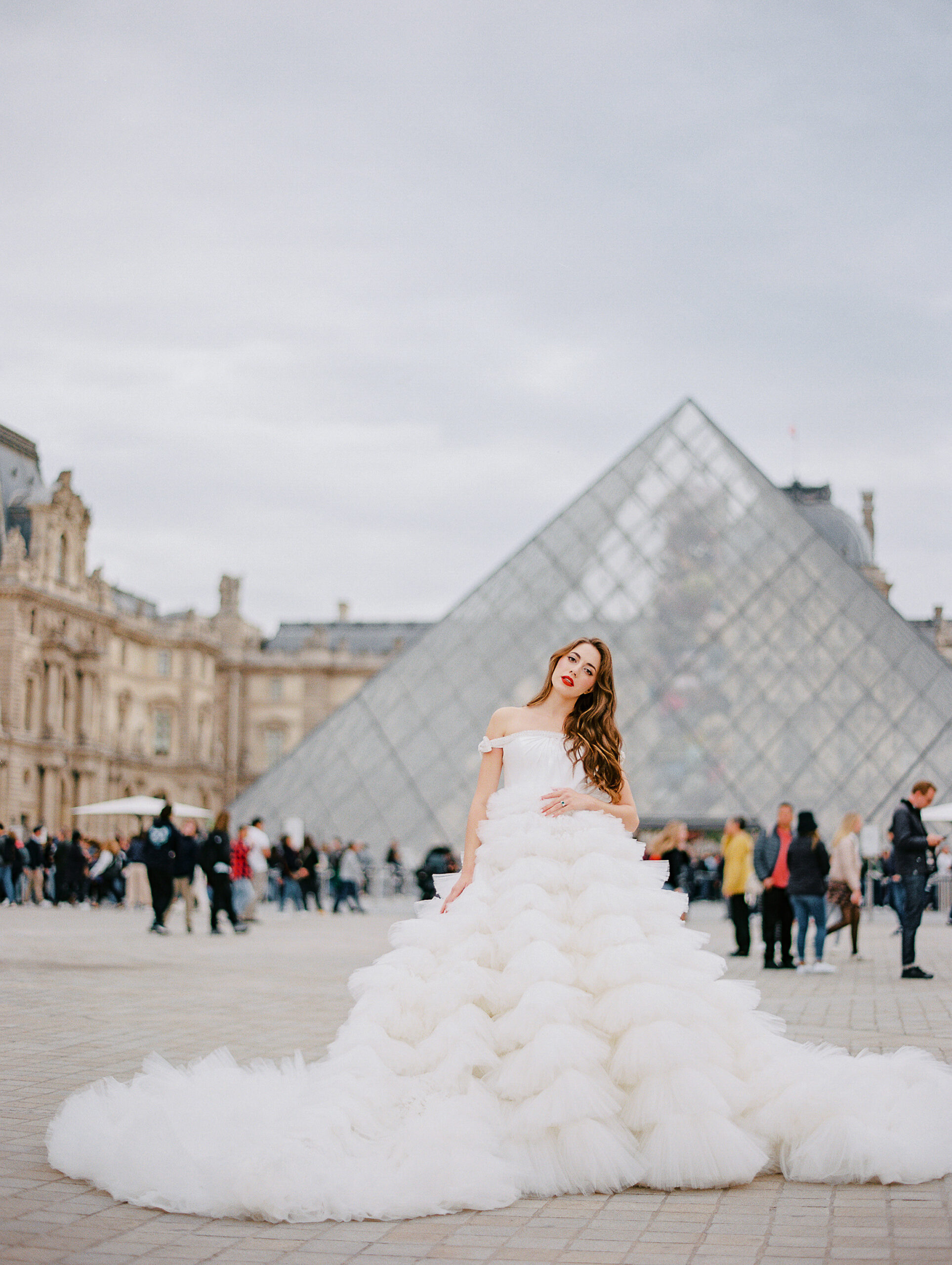 A woman in a voluminous white gown stands before the Louvre Pyramid in ...