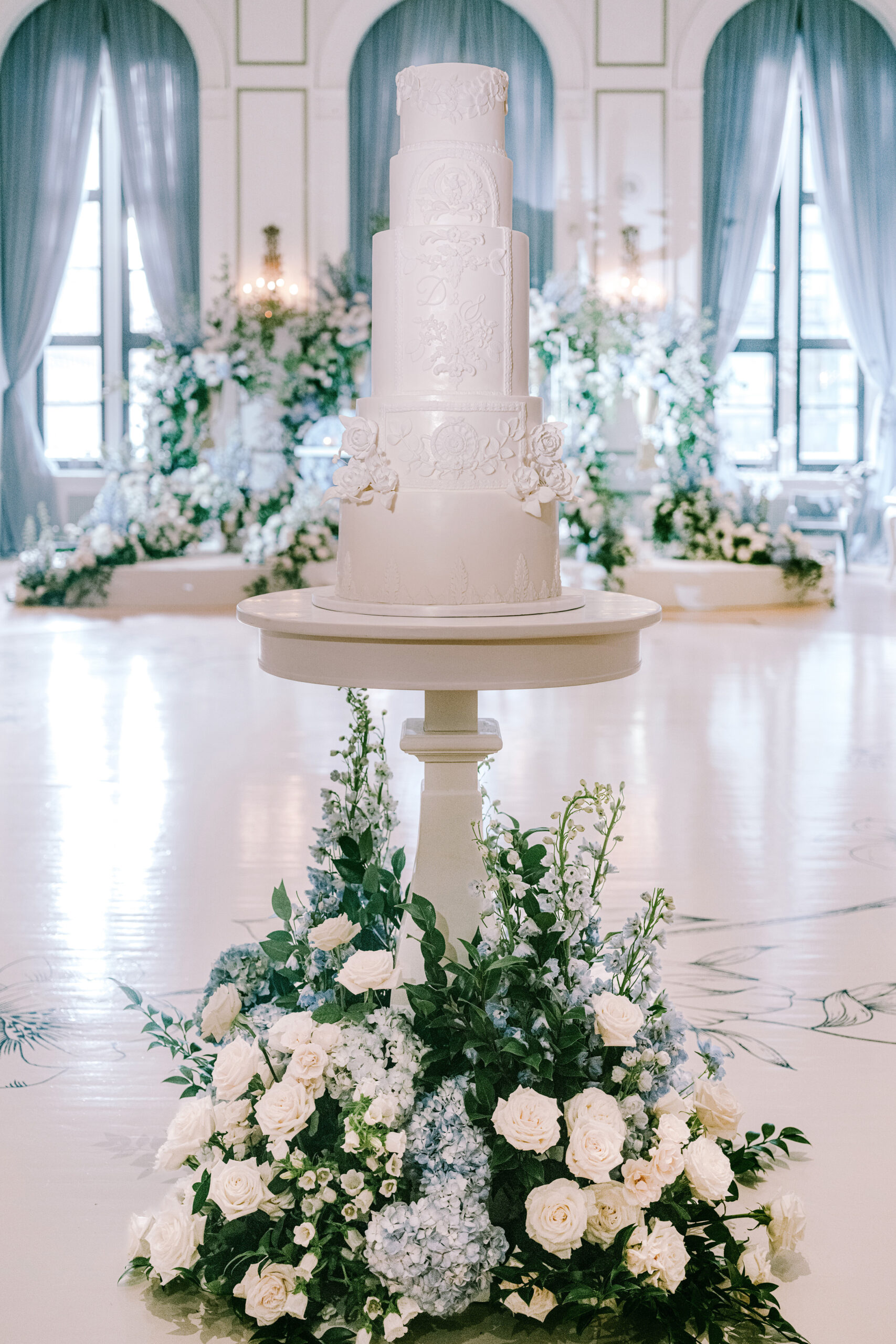 A tall, elegant white wedding cake with intricate designs sits on a ...