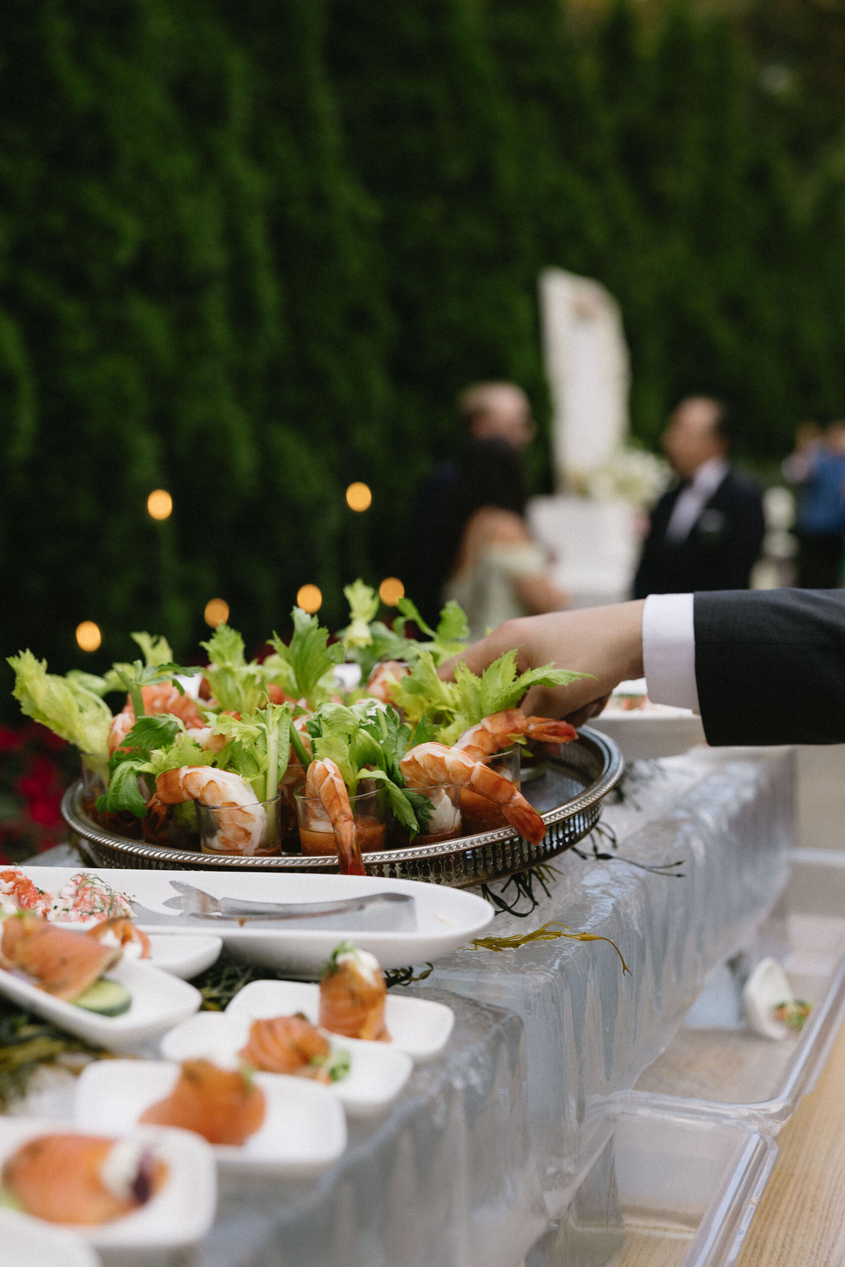 A person in a suit reaches for shrimp cocktail from a platter at an ...
