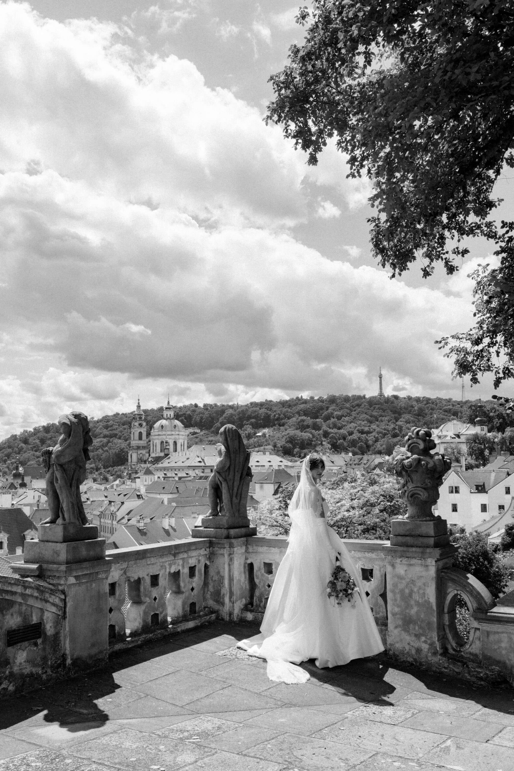 A bride in a wedding gown and veil stands on a terrace overlooking a ...