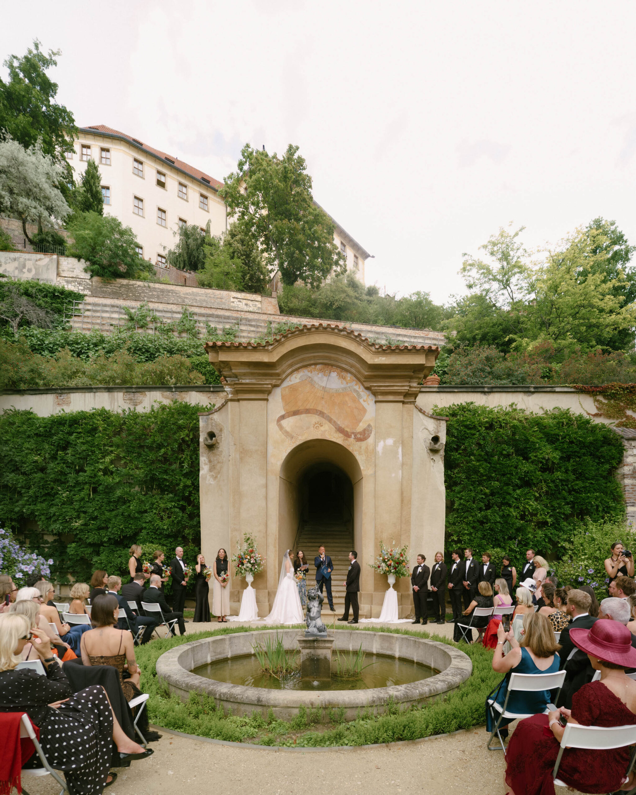 A luxury Prague wedding unfolds before an ivy-covered arch, with the ...