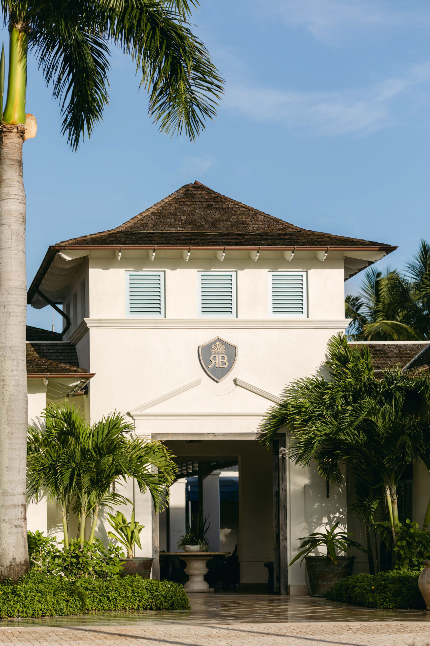 A white building with a dark peaked roof, blue shutters, and palm trees ...