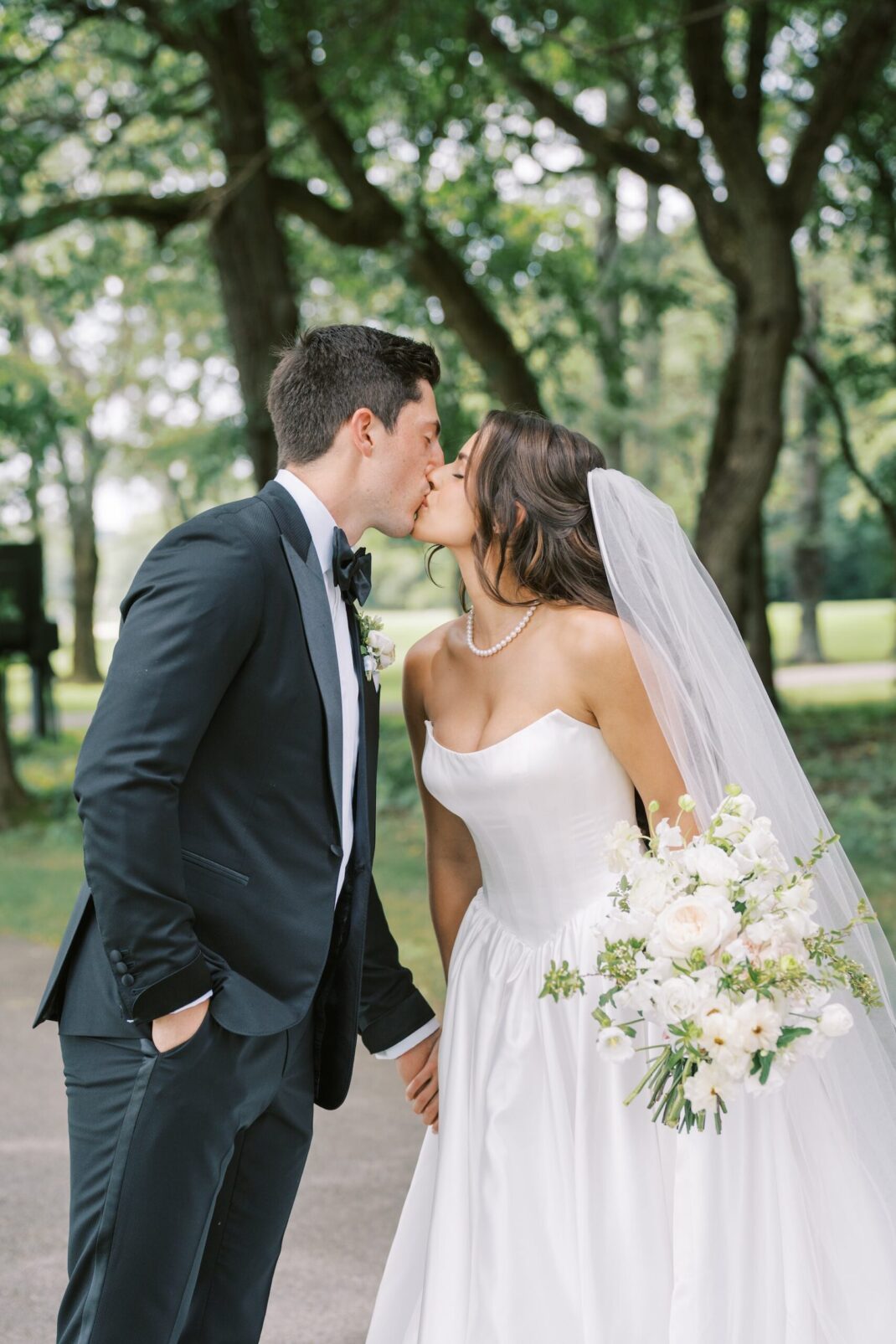 A bride in a white gown and veil kisses a groom in a black suit ...