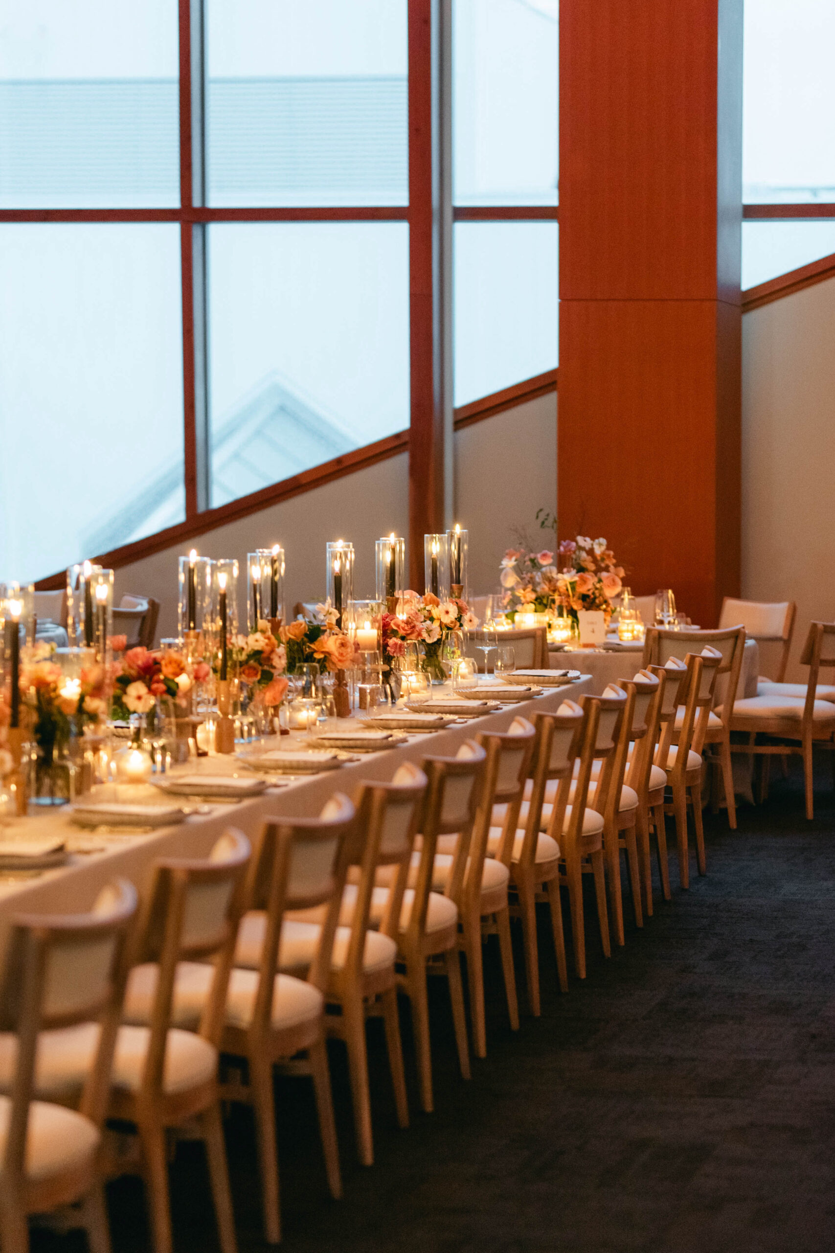 A long, elegant dining table set with white plates, candles in glass ...