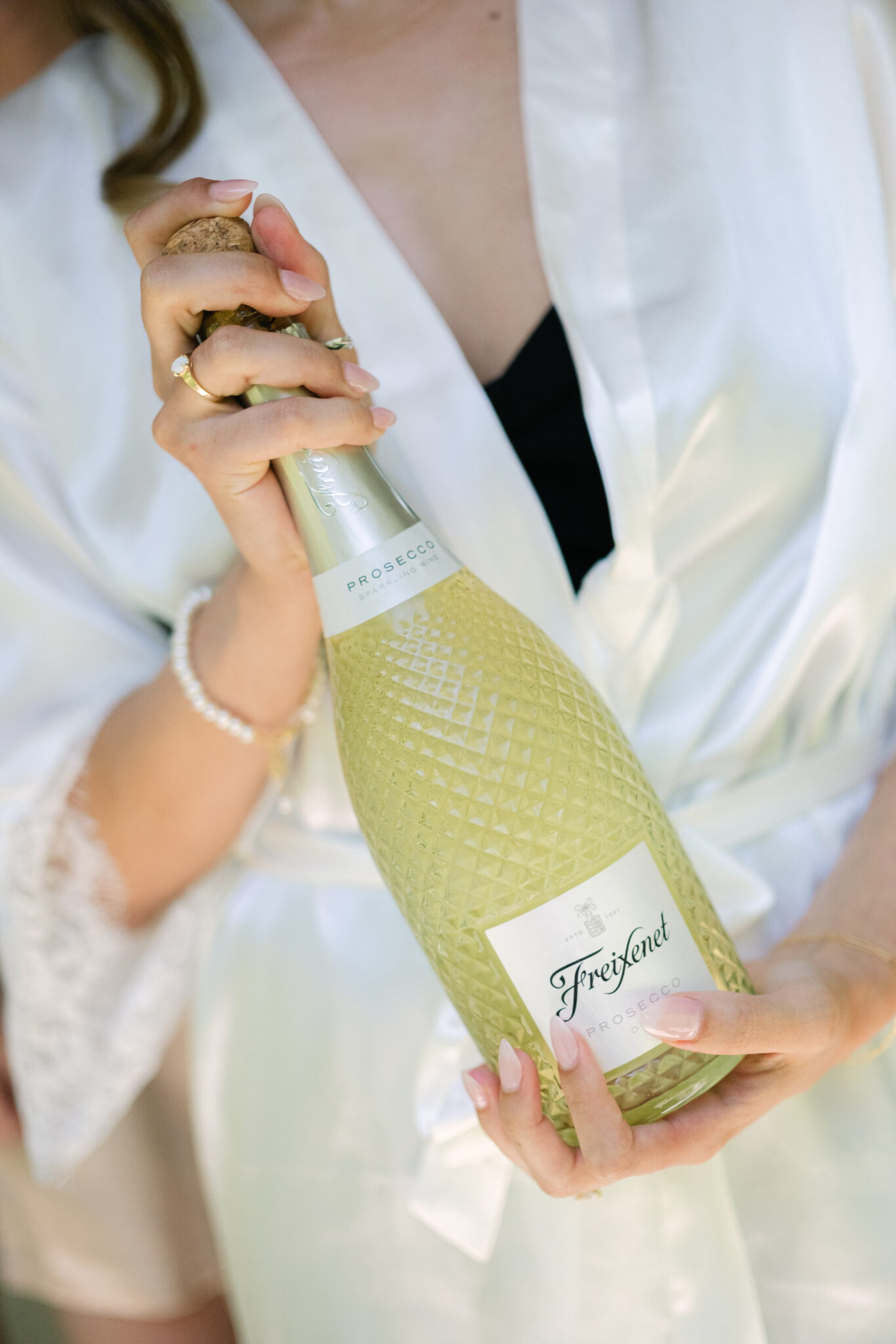 A woman in a white robe holds an unopened bottle of Freixenet Prosecco ...