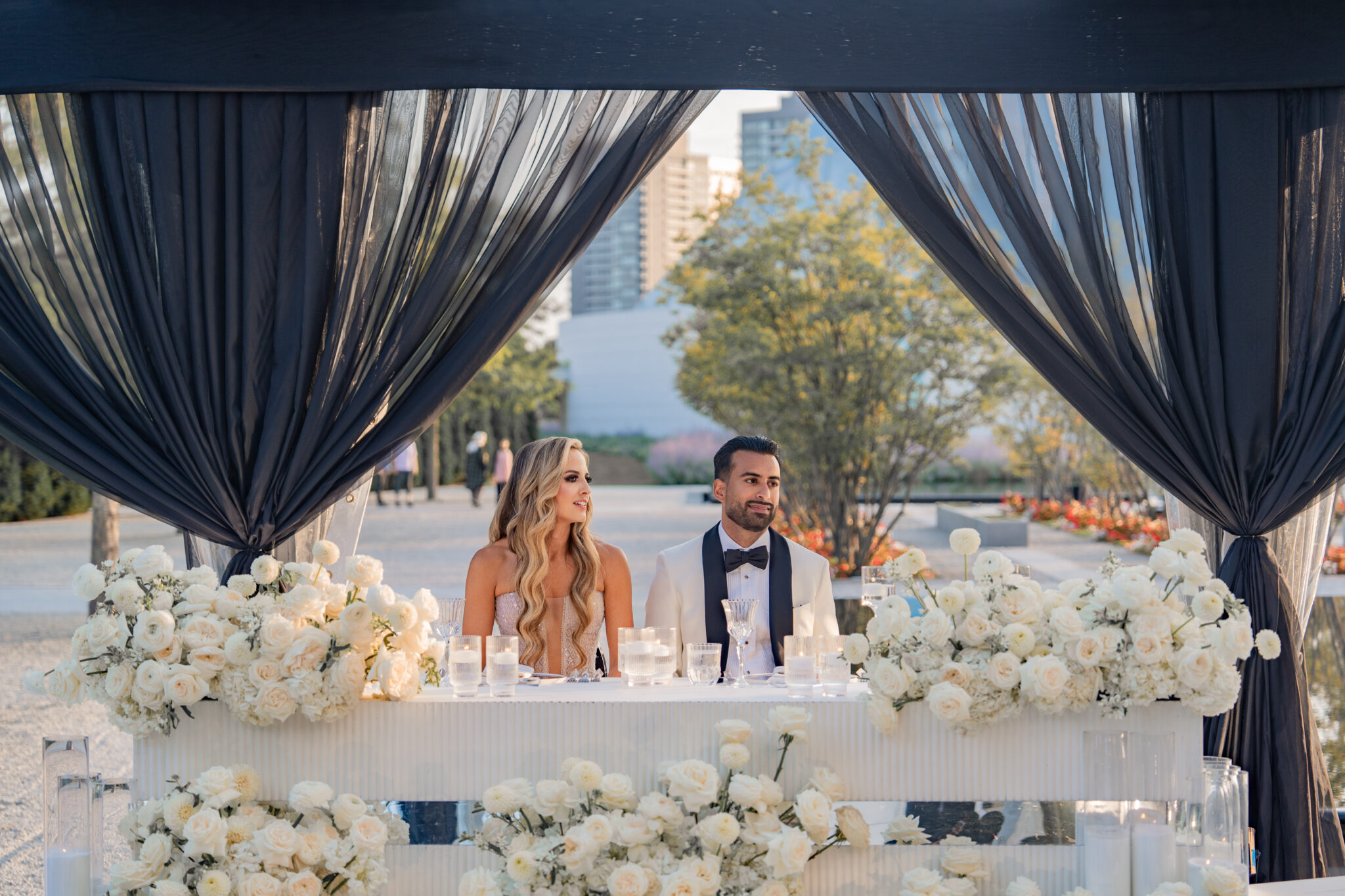 A bride and groom sit together at a flower-adorned table under a black ...