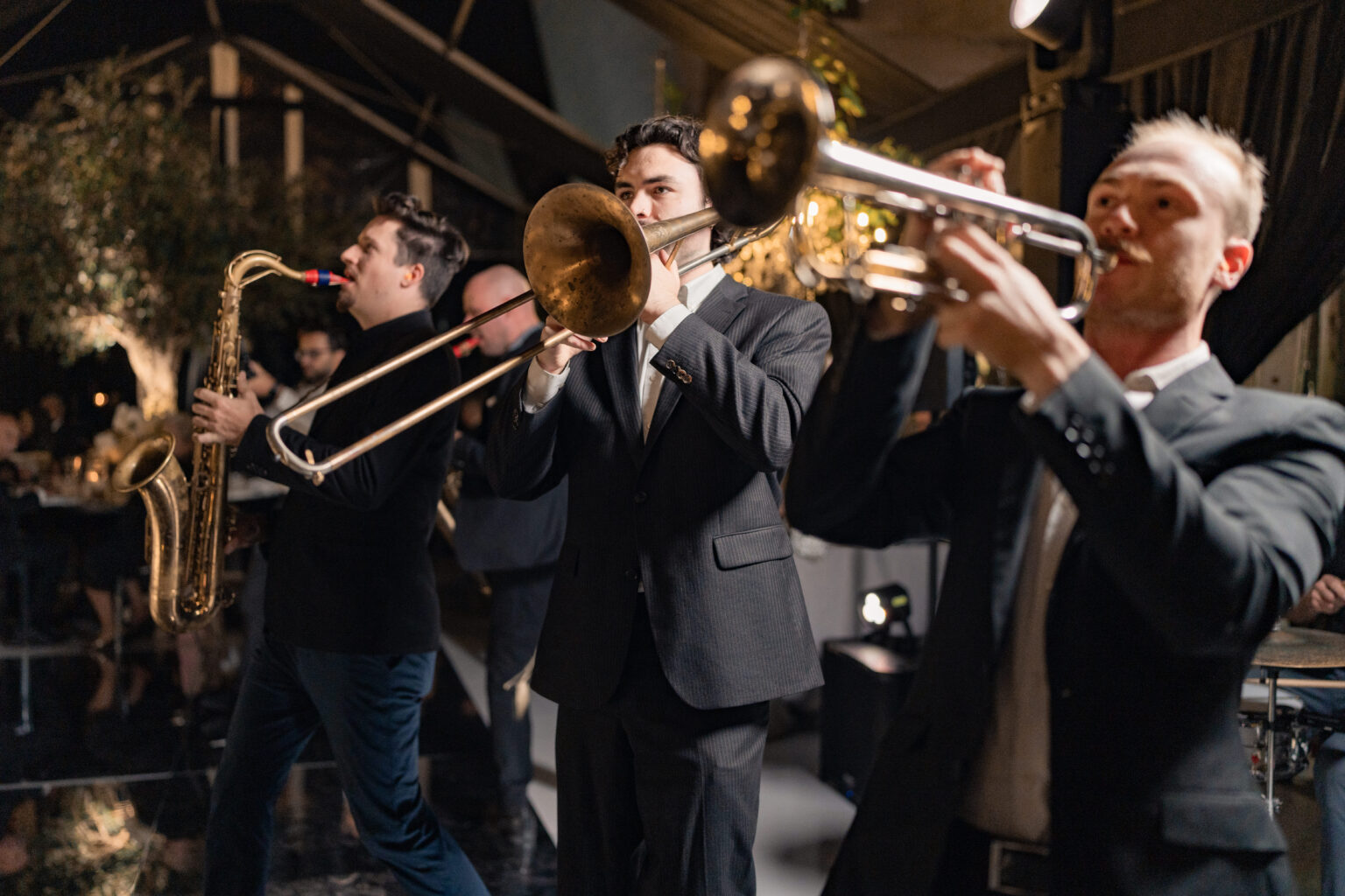 Three musicians in suits play saxophone, trombone, and trumpet at an ...