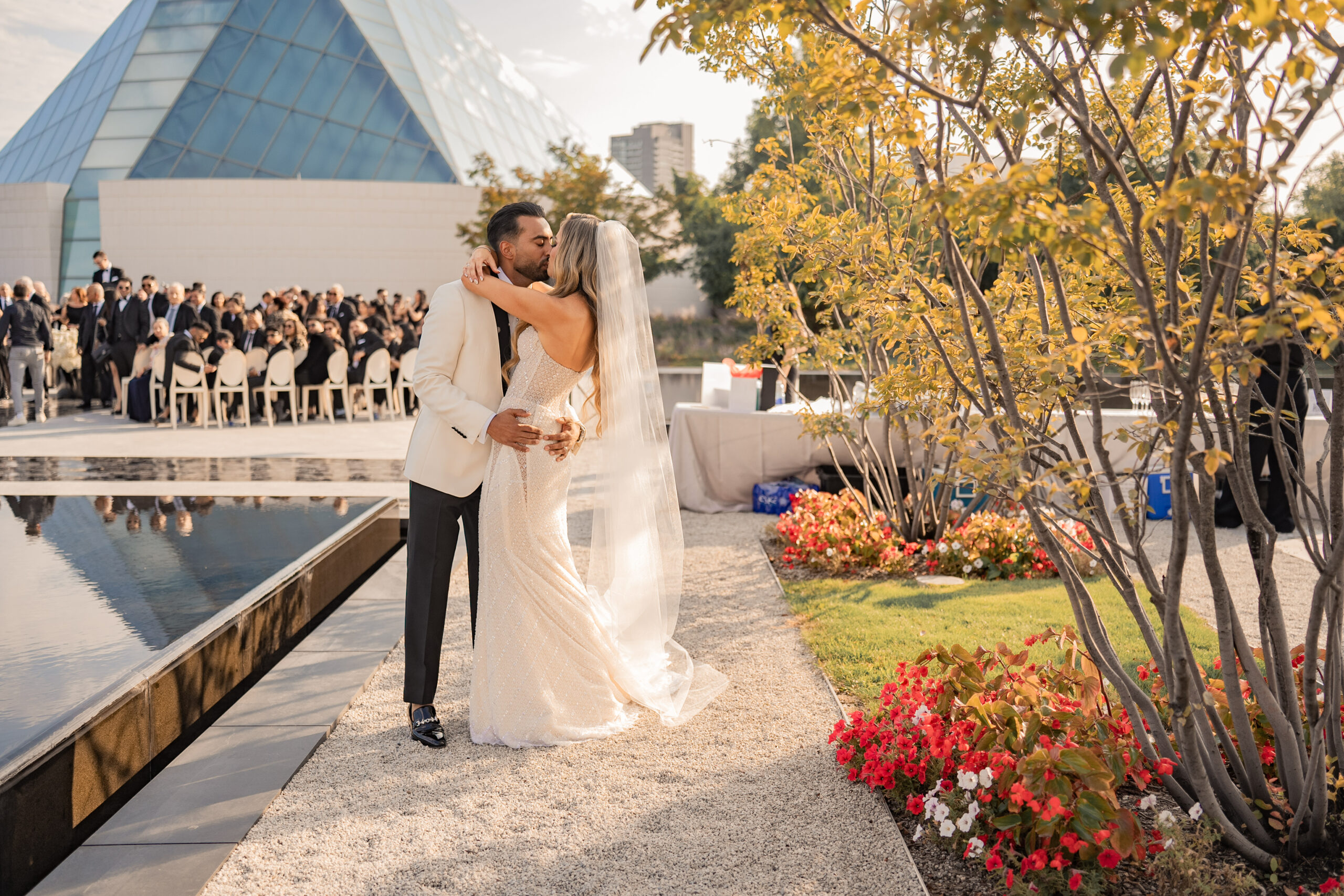 A bride and groom share a kiss outdoors beside a reflecting pool at ...