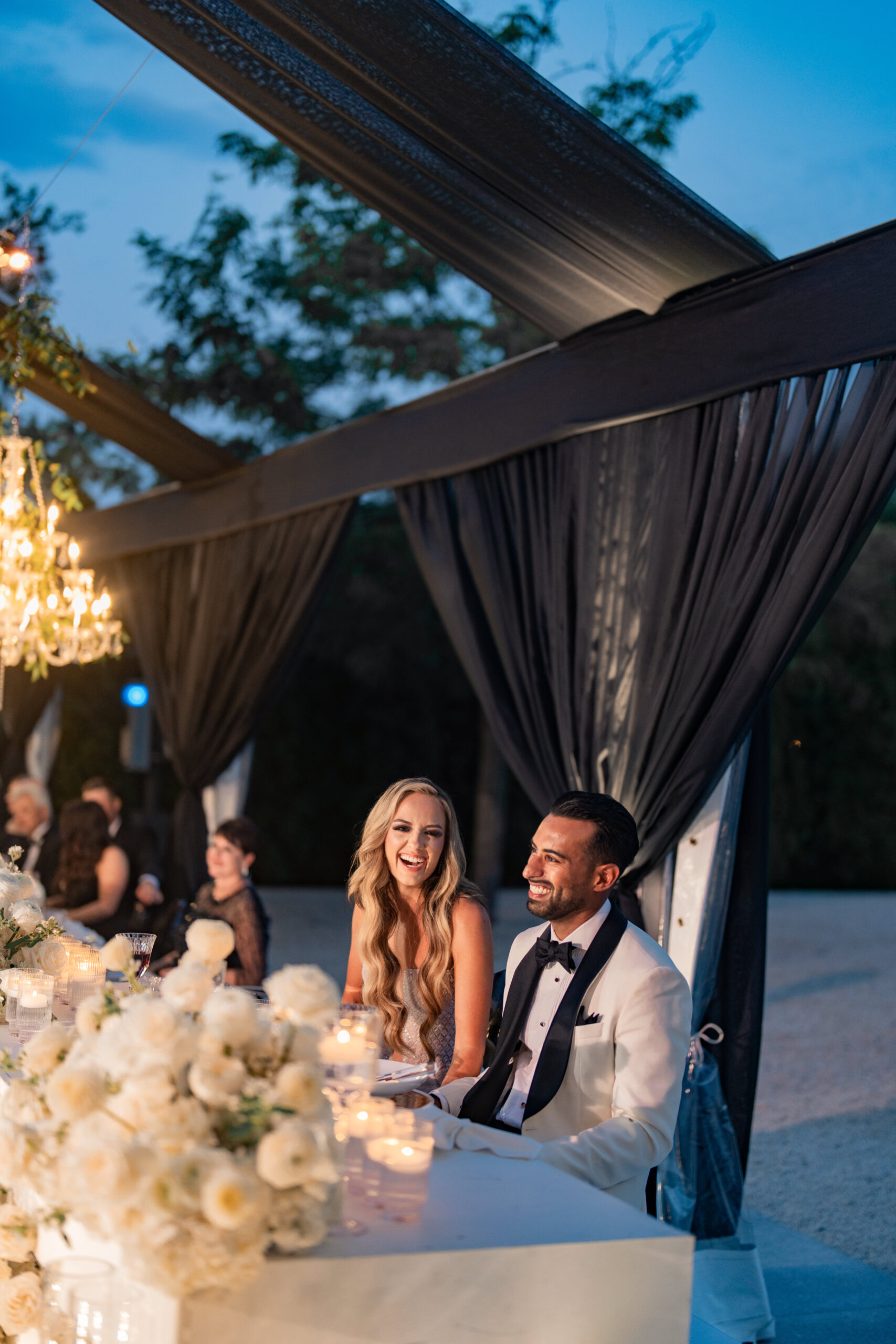 A bride and groom sit together at a decorated table, smiling and ...