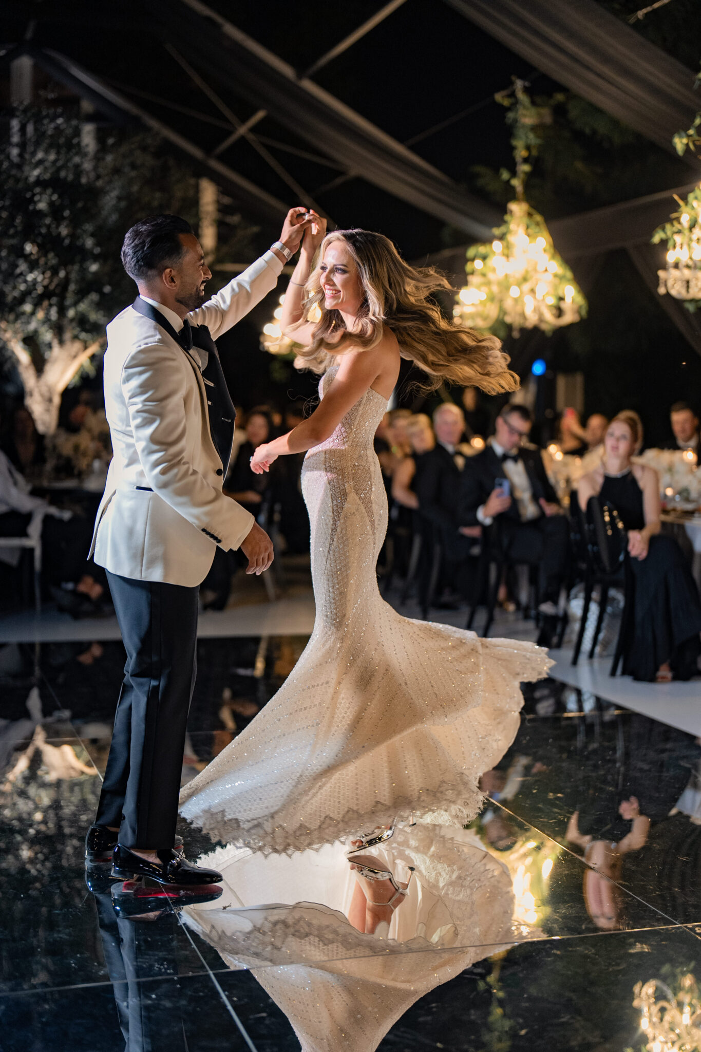 A bride and groom dance joyfully on a reflective floor at their elegant ...