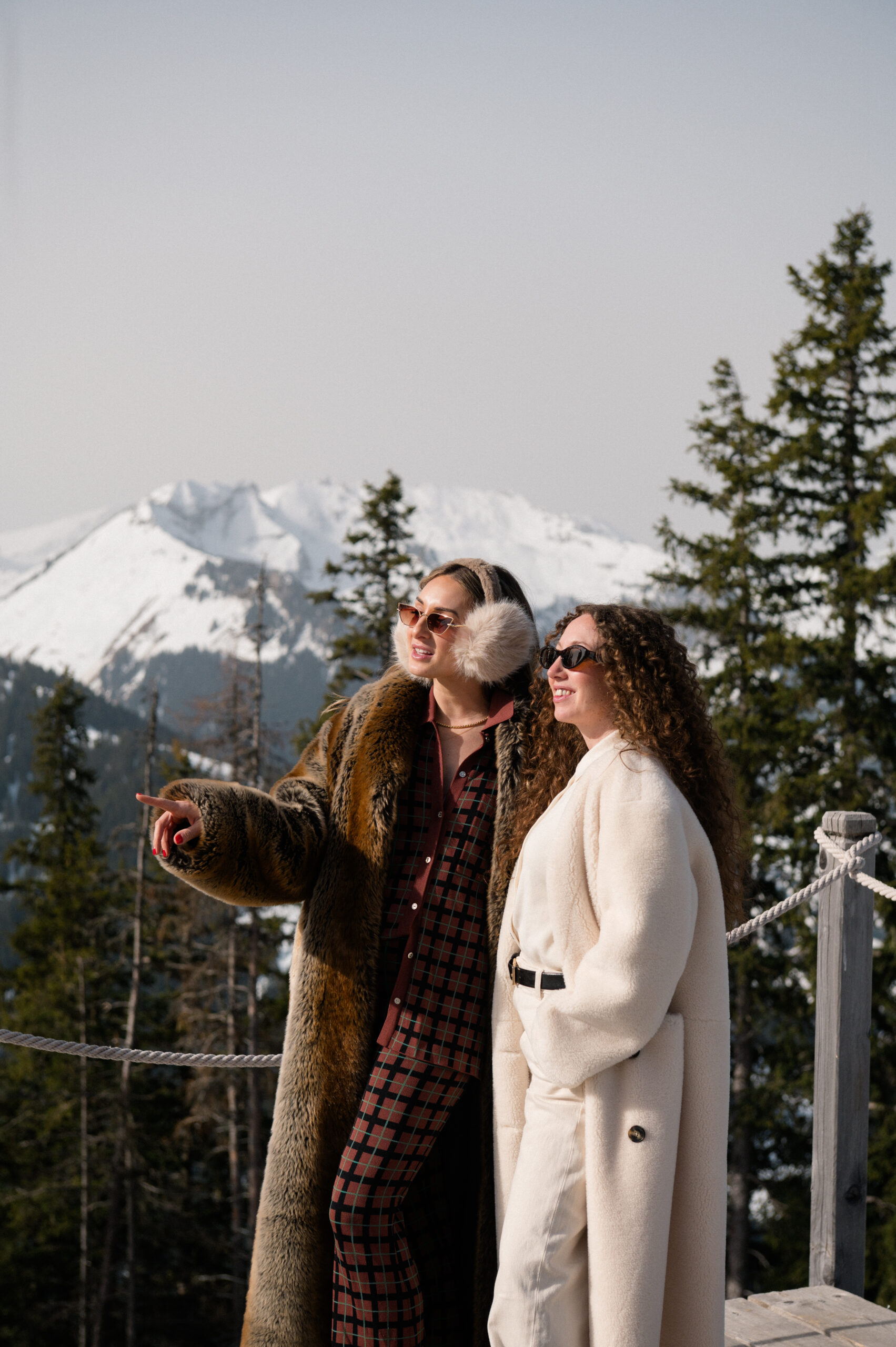 Two people in stylish winter outfits and sunglasses stand outdoors ...