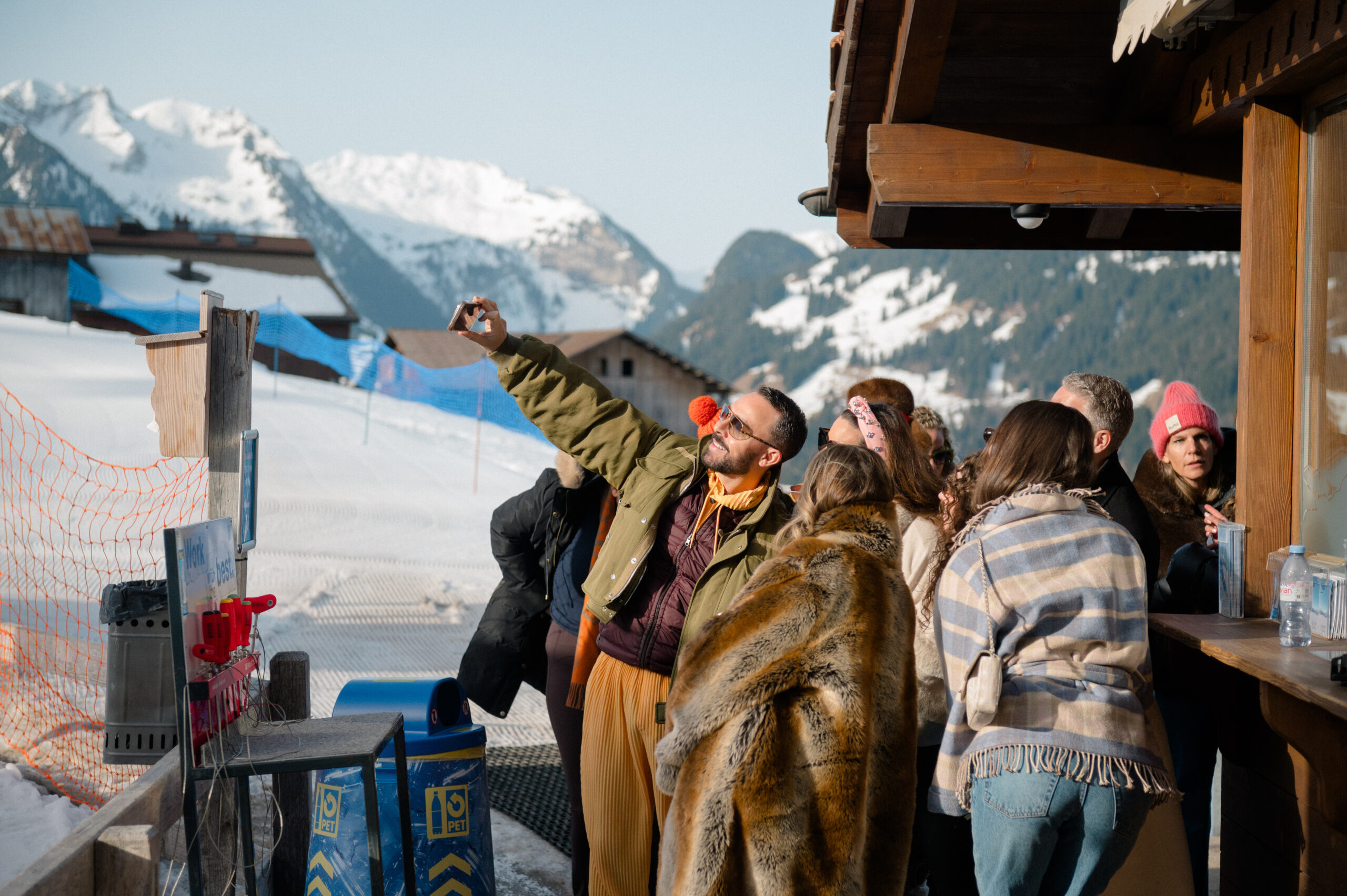 A group of people in winter clothing gather outside a wooden building ...
