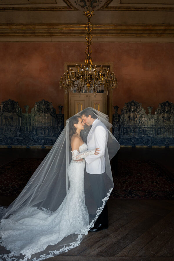 A bride and groom embrace and smile at each other under a sheer veil in ...