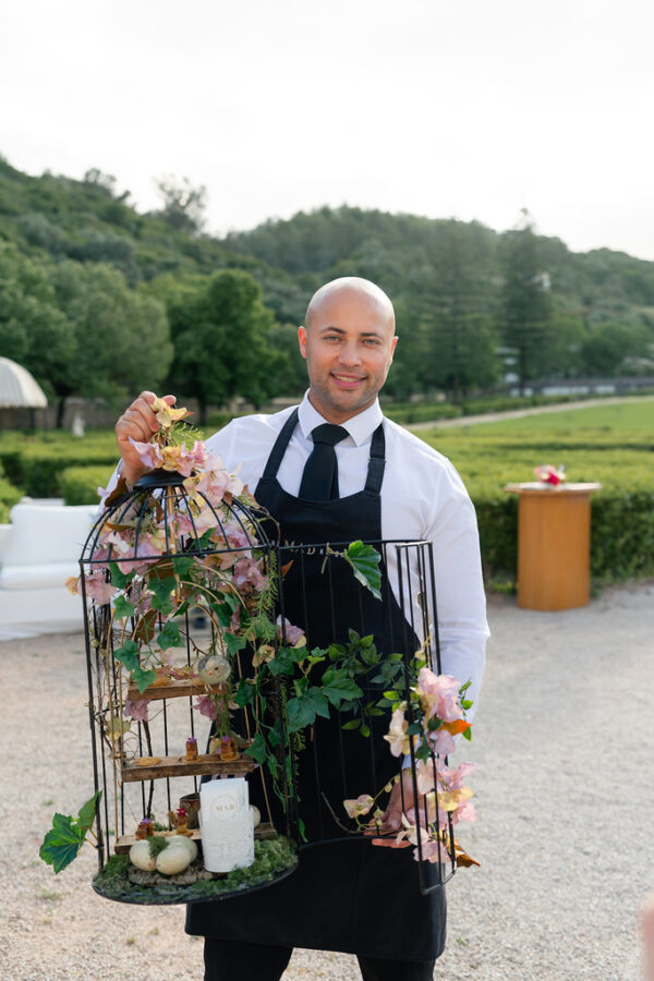 A man in a white shirt, black tie, and apron stands outdoors at a ...